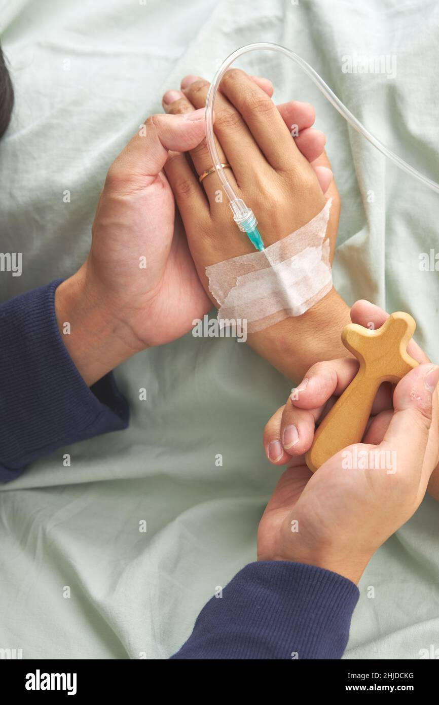 Vertical shot of a man holding her wife's hand connected to an IV drip ...