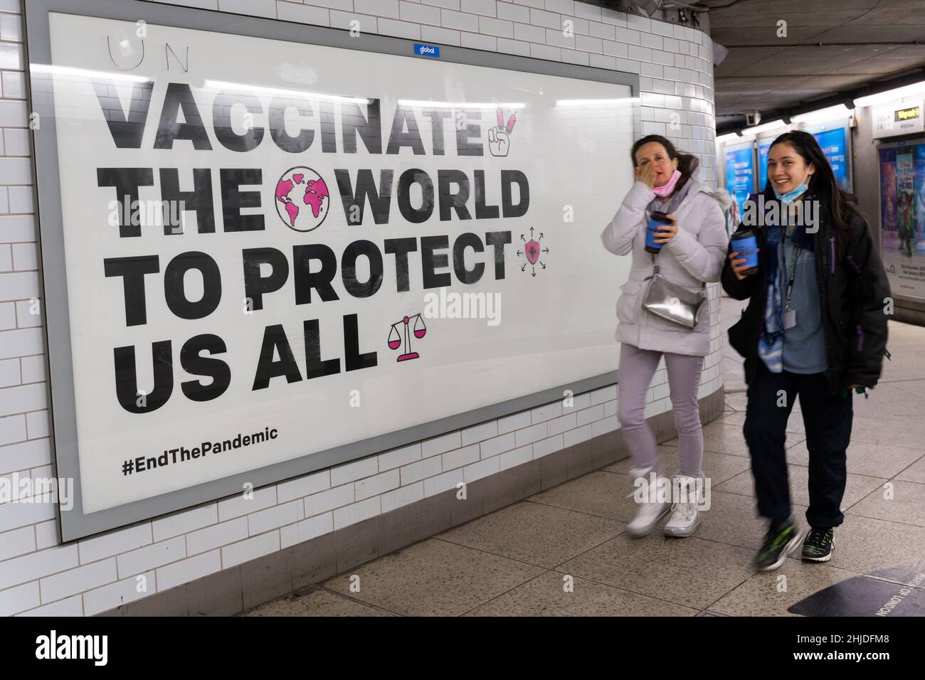 two women walks past poster on the billboard showing "vaccine the world ...