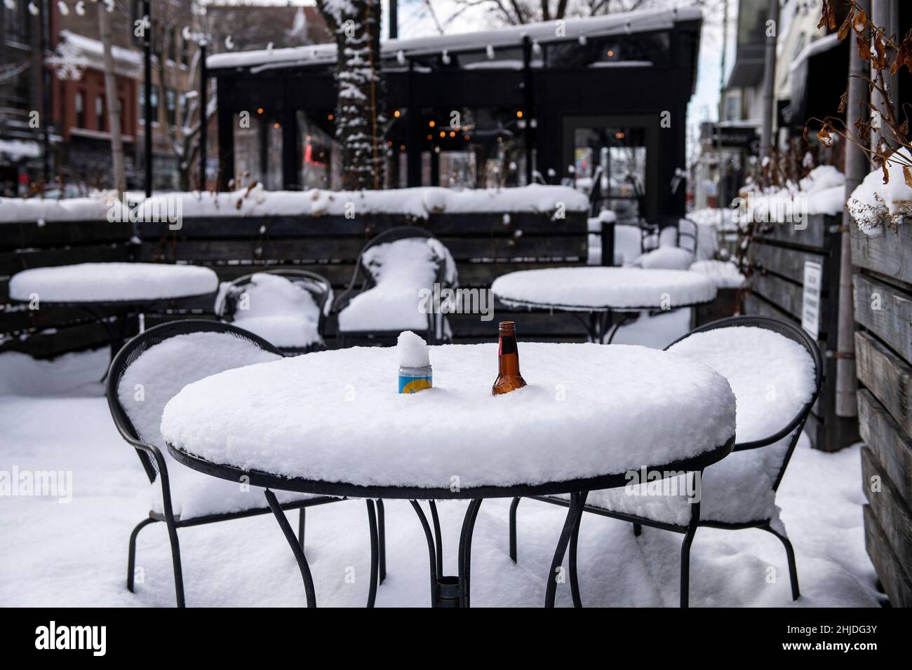 A beer can and bottle are covered in snow at an outdoor eating area ...