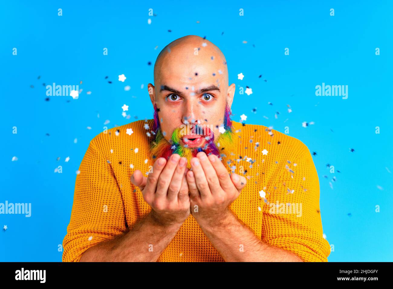 handsome man with raindow in beard and yellow sweater blowing glitter ...