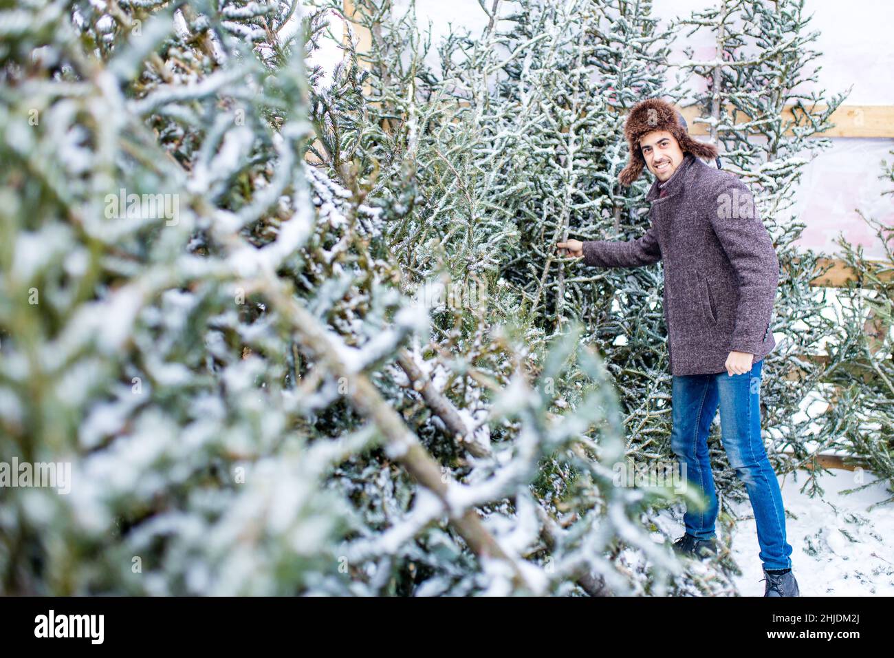indian man in stylish wool coat buys a Christmas tree outdoors snow ...