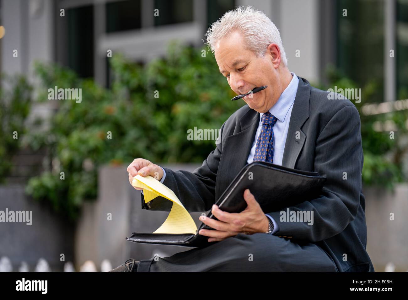 Businessman going through his notes with pen in mouth Stock Photo - Alamy