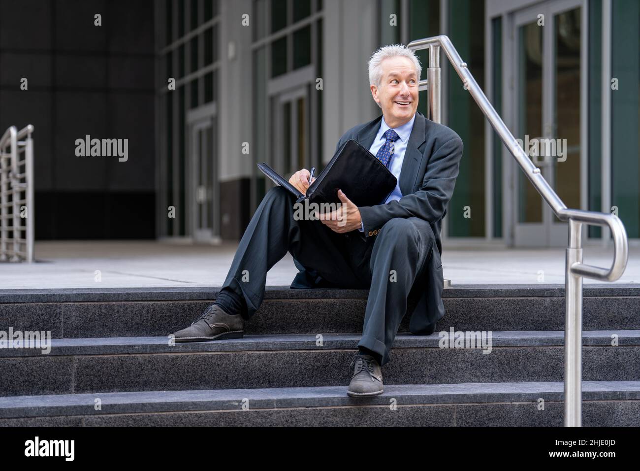 Successful old businessman sitting on a staircase by an office building ...