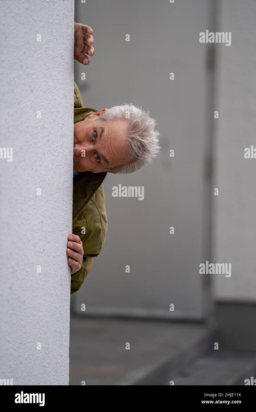 Businessman peeking his head out sideways from behind the building ...
