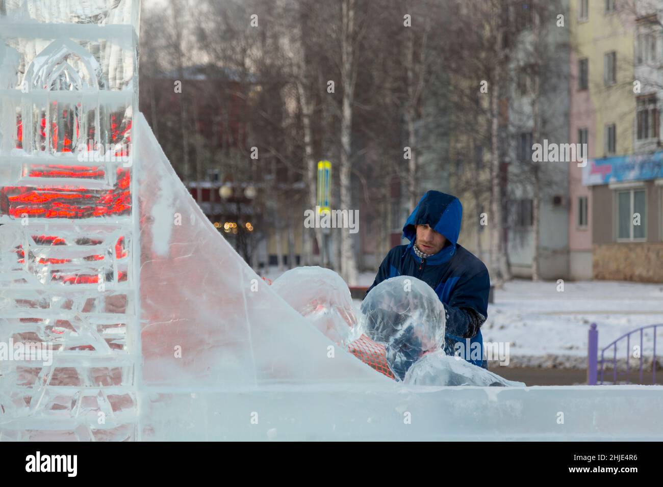 A sculptor carves a round ice ball out of a block of ice with a chisel ...