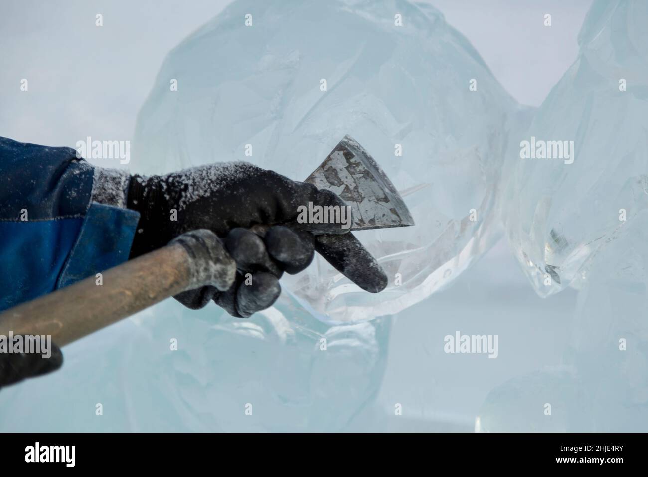 The master's hands beat off a piece of ice from an ice block with a ...