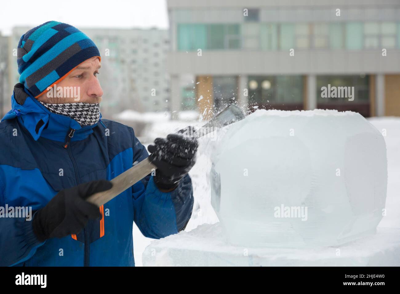 A sculptor carves a round ice ball out of a block of ice with a chisel ...