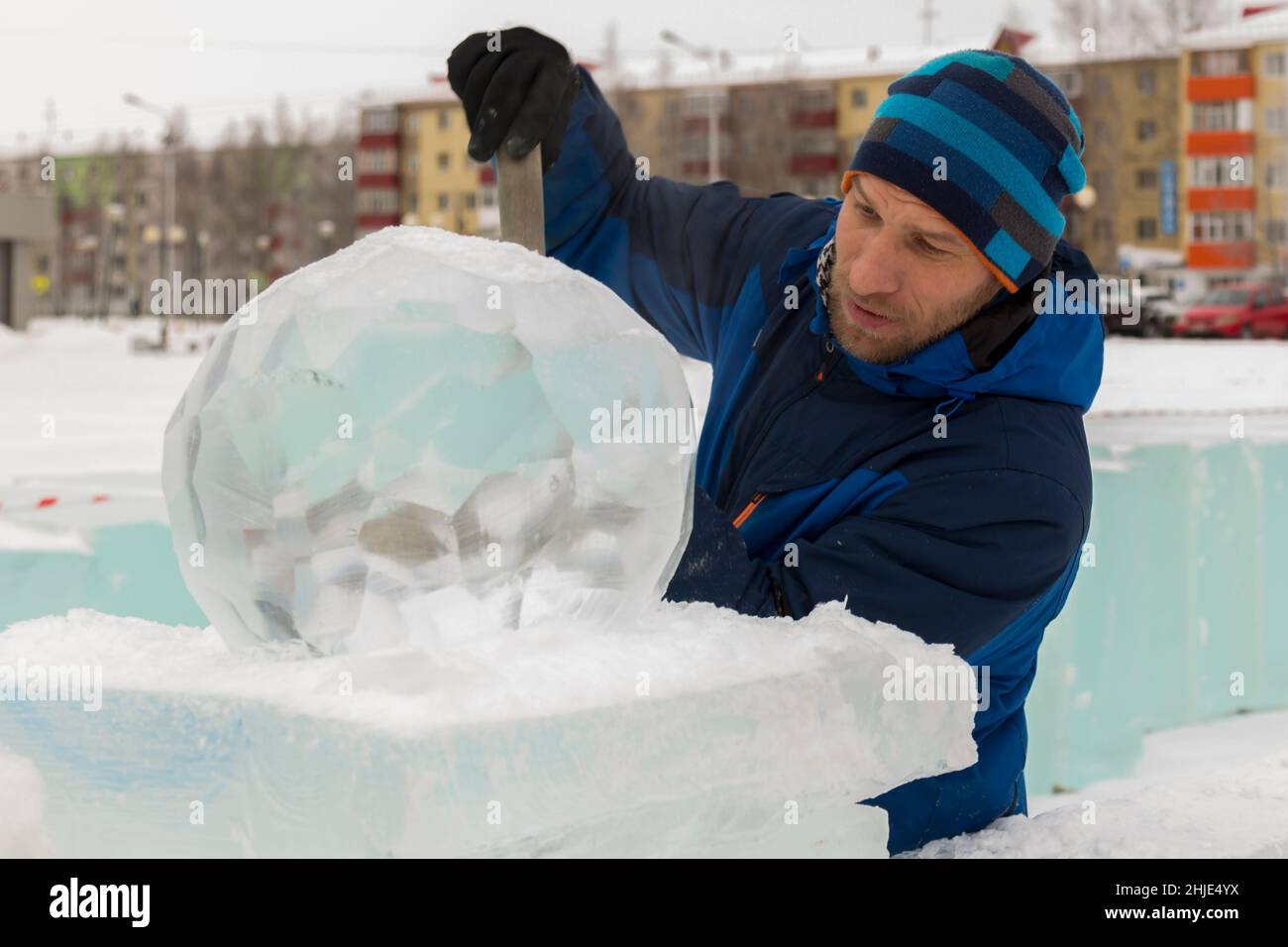 A sculptor carves a round ice ball out of a block of ice with a chisel ...