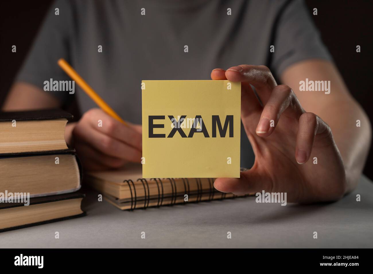Female hand holding word Exam on yellow sticker Stock Photo - Alamy