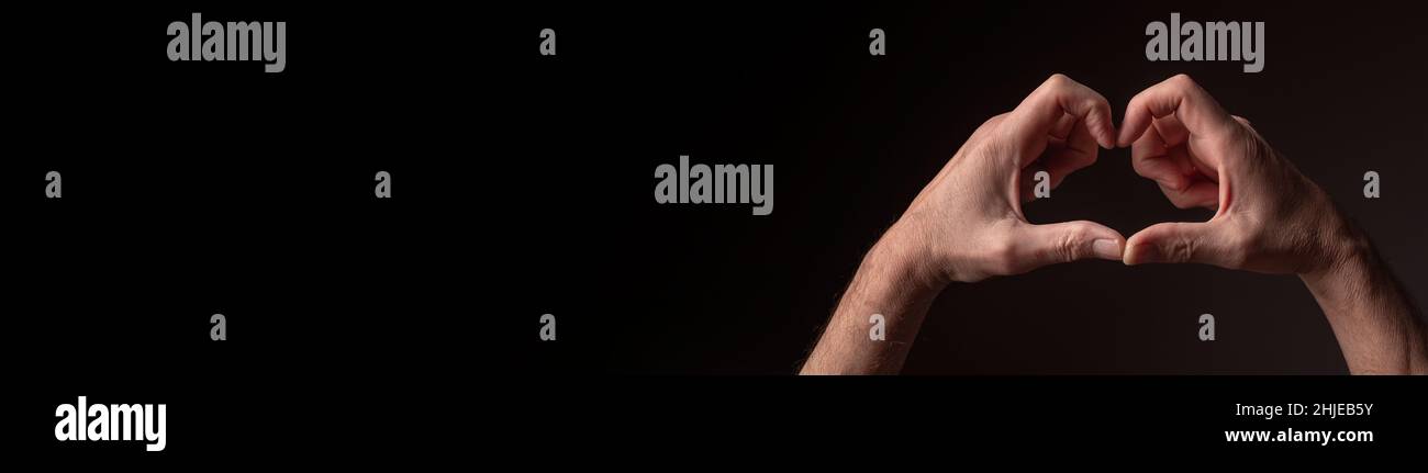Heart-shaped male hands as peace and hope symbol over black background ...
