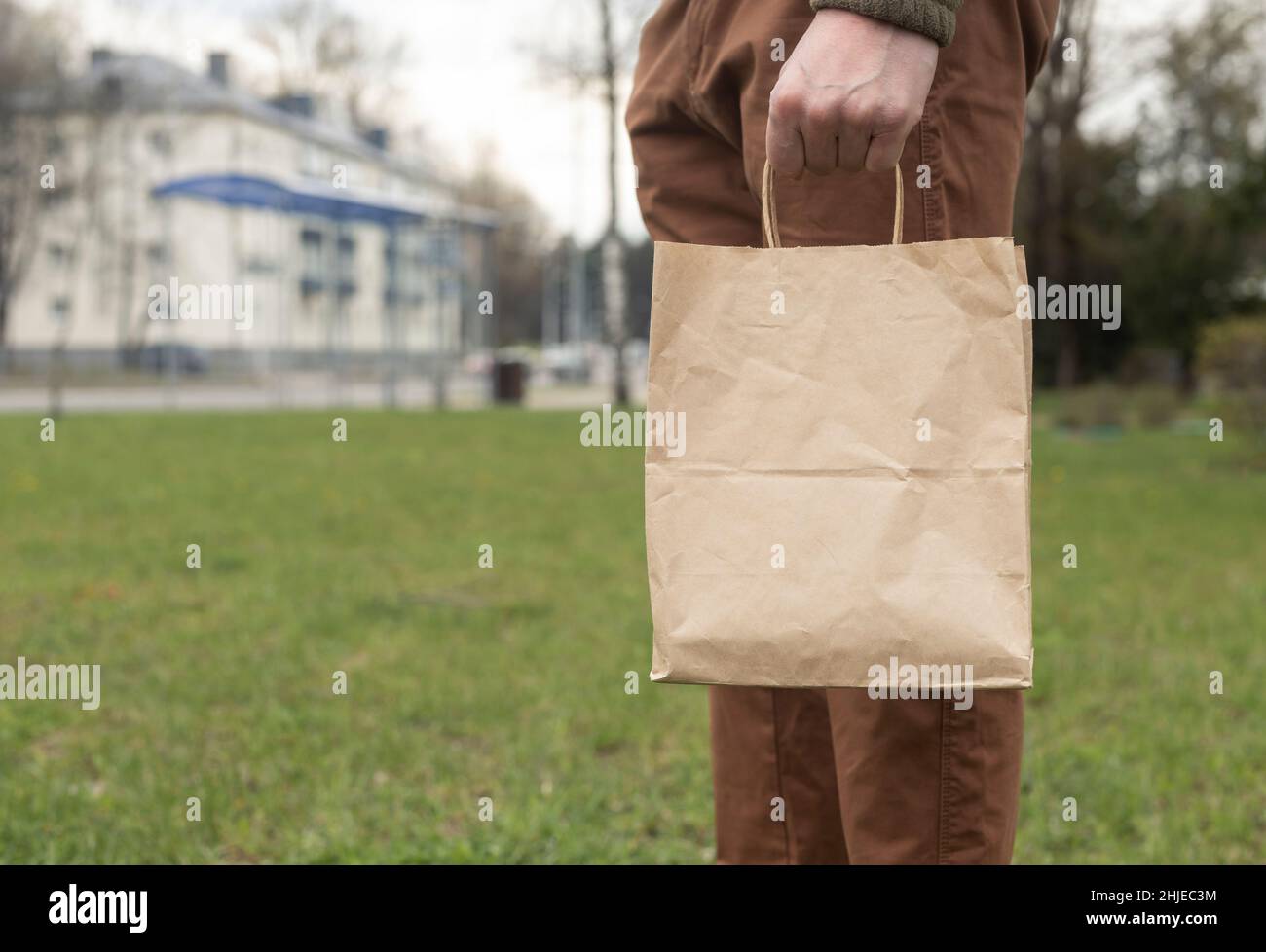Male hand close up holding brown craft pack in hand on city and grass ...