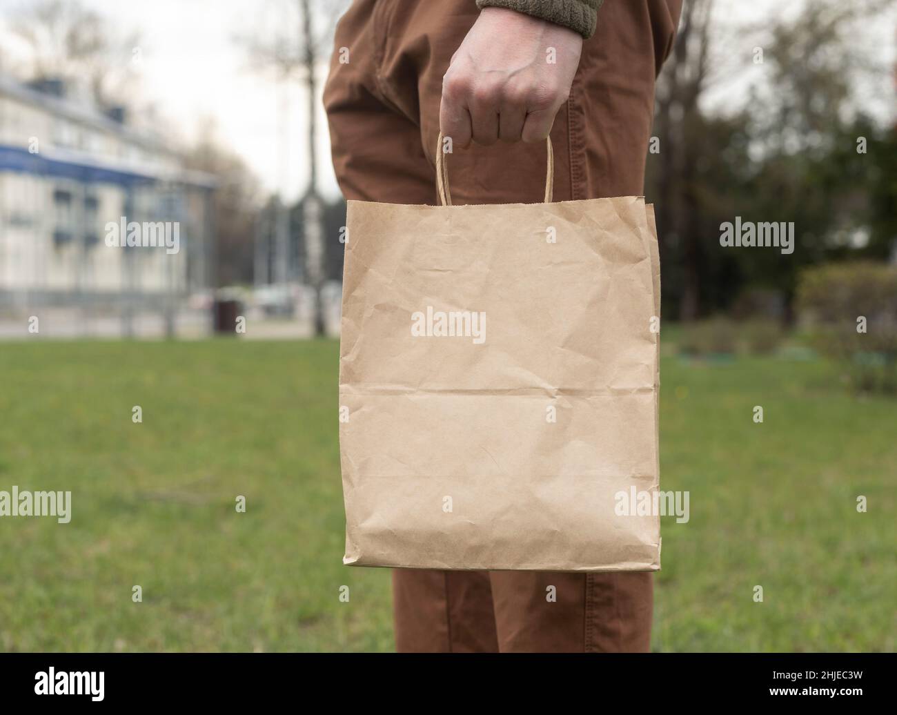 Hand with brown craft pack or packet in hand on city and grass ...
