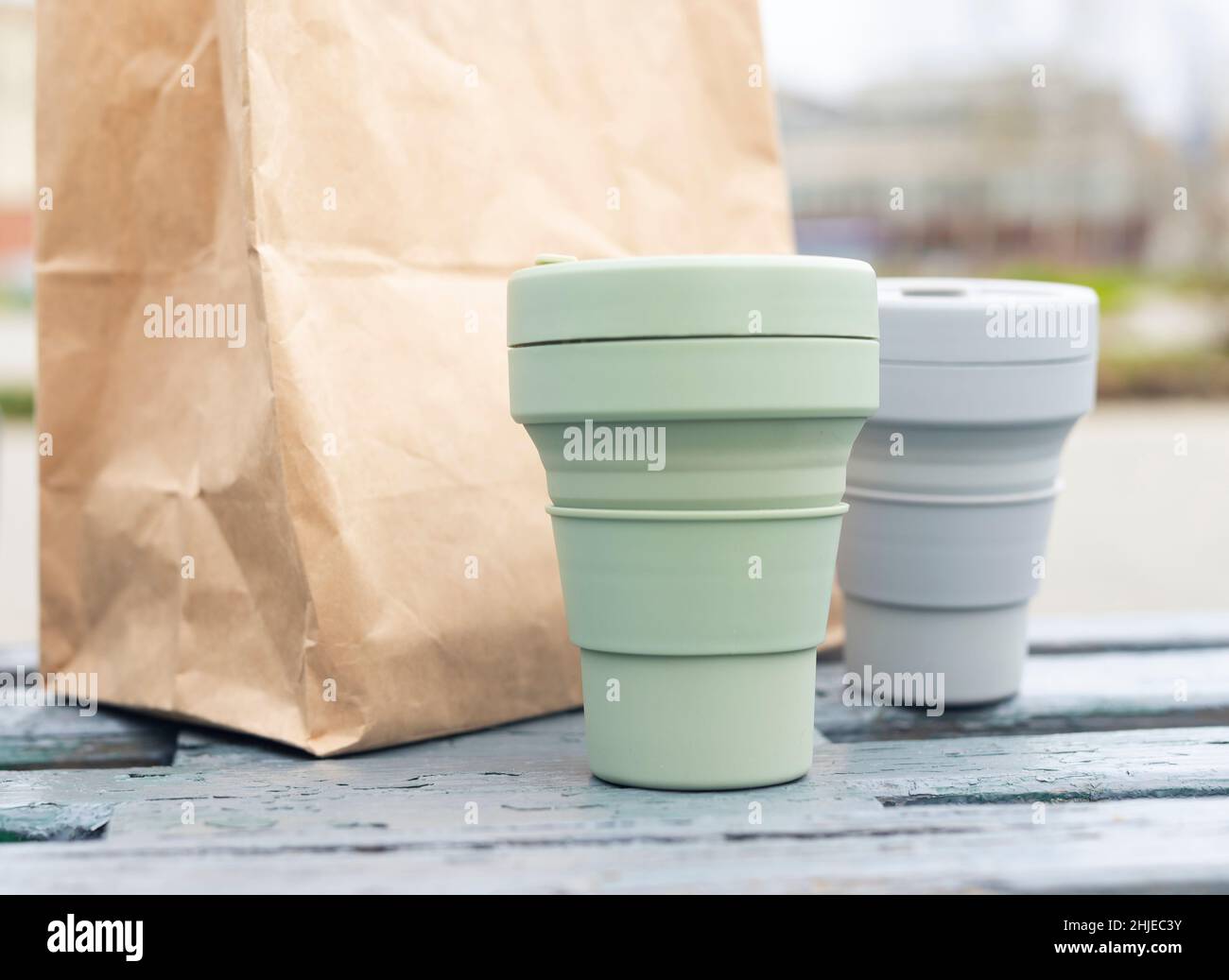Two collapsible eco cups and craft parcel on city park bench. Reusable ...