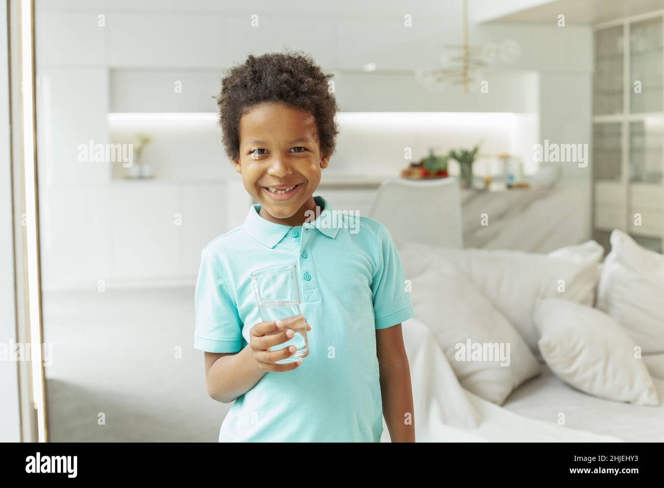 Cute little boy smiling and drinking water from glass on white ...