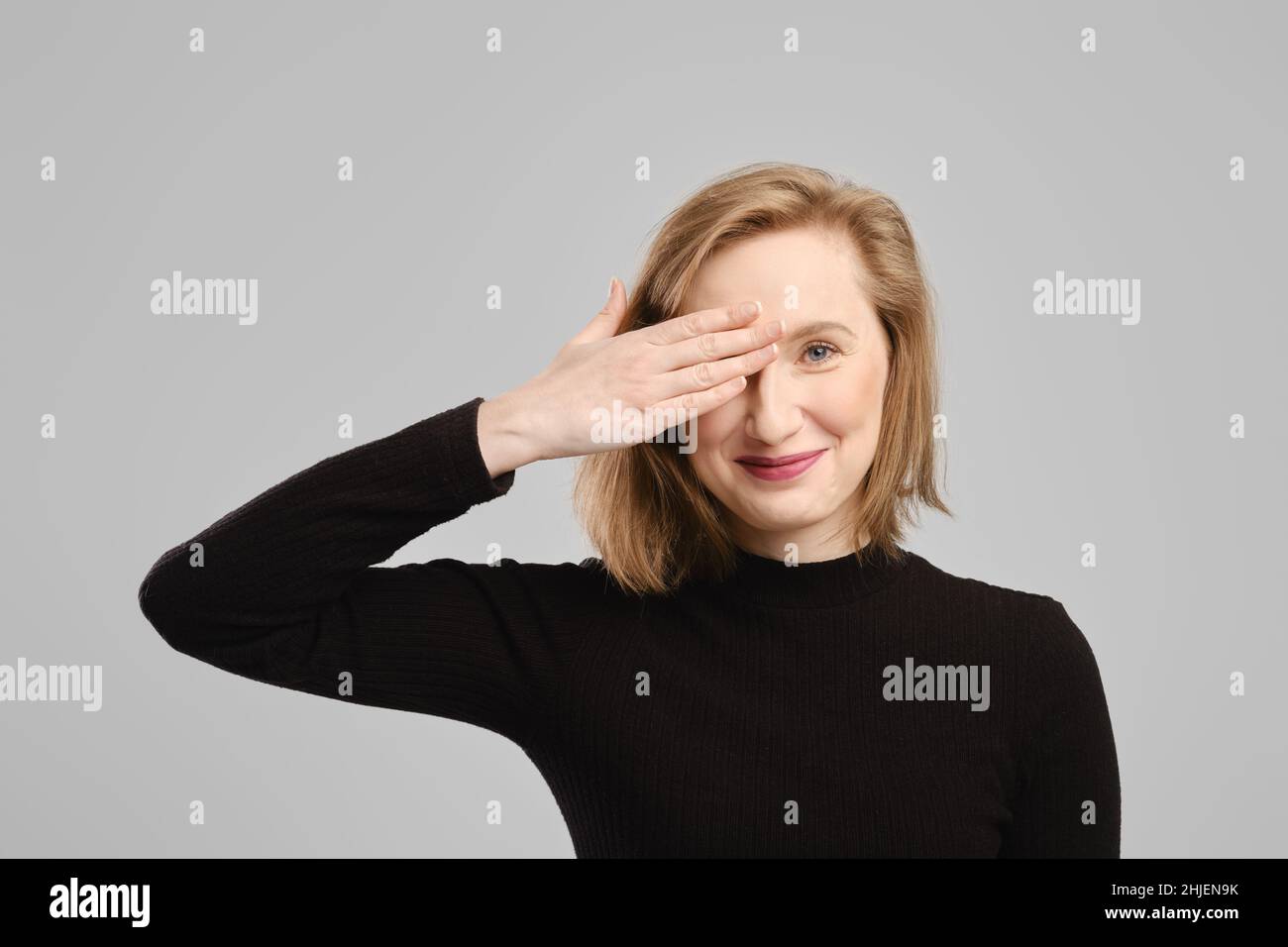 Smiling woman covering one eye over grey studio background Stock Photo ...