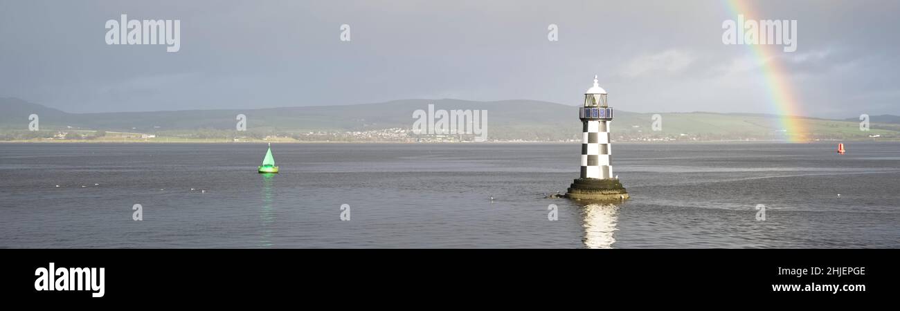 Bright rainbow high in sky over lighthouse in sea during dark storm ...