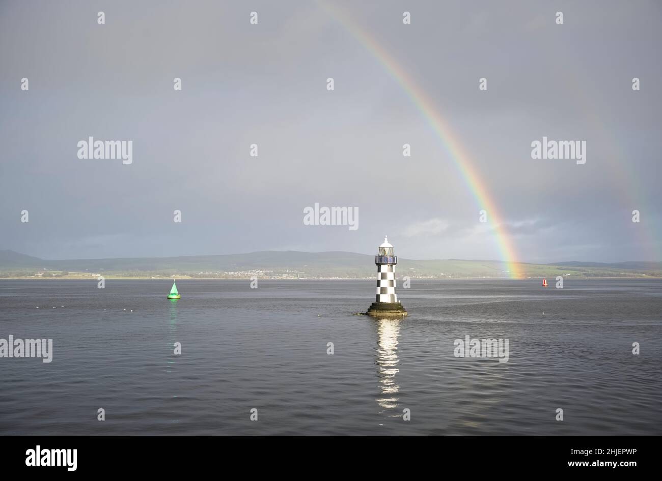 Bright rainbow high in sky over lighthouse in sea during dark storm ...
