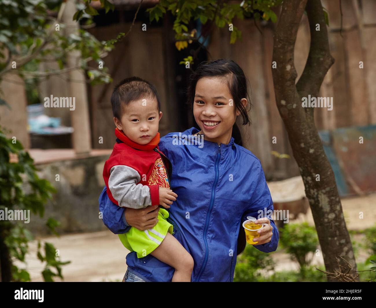 A young smiling Vietnamese girl teenager holds her little brother in ...