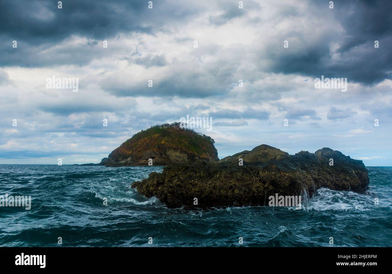 Rock Island over stormy blue sea water and overcast sky Stock Photo - Alamy