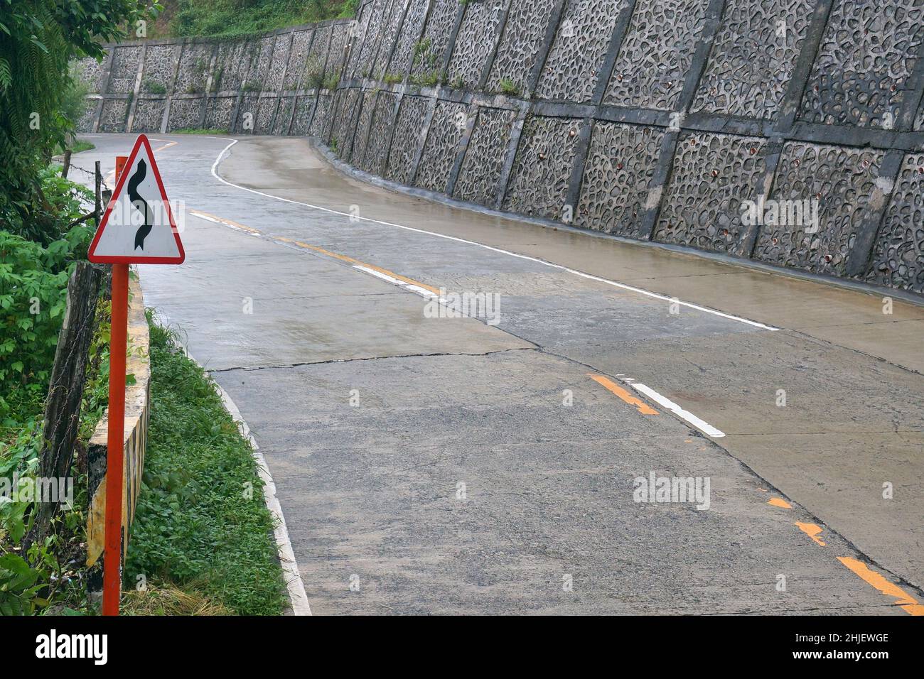 Road sign in the edge of wet winding road. An early warning sign for ...