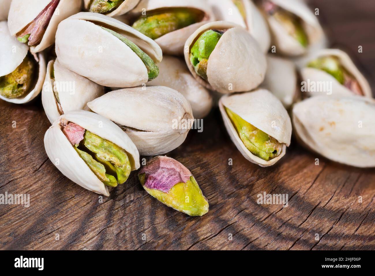 Beautiful roasted salted pistachio nut kernels in split shells on wood detail. Pistacia vera ...