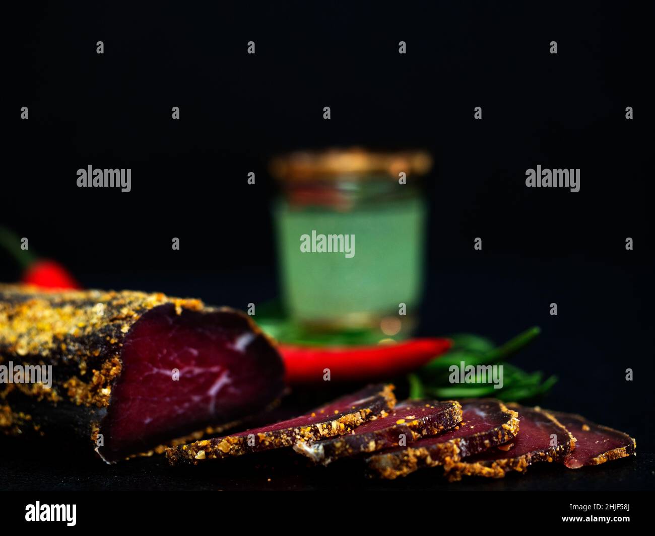 Pieces of basturma with hot pepper and rosemary on black table ...