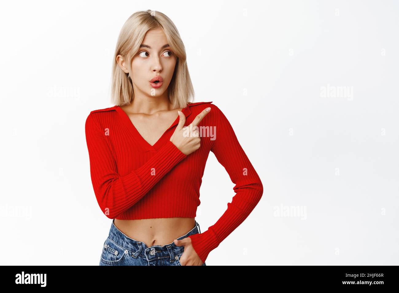 Excited young woman looks curious, points at upper right corner, looks ...