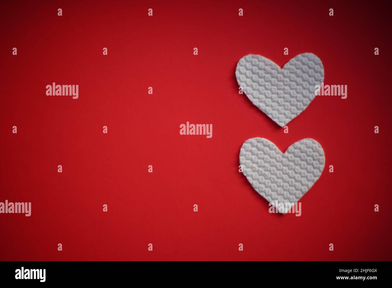 Two white fabric hearts on red table. Copy space. Valentine's day theme ...
