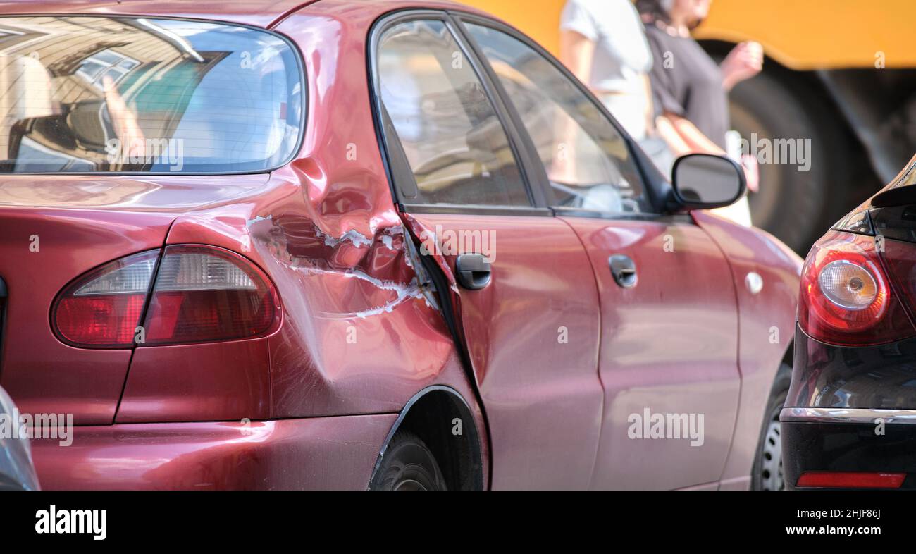 Dented car with damaged body parked on city street side. Road safety ...