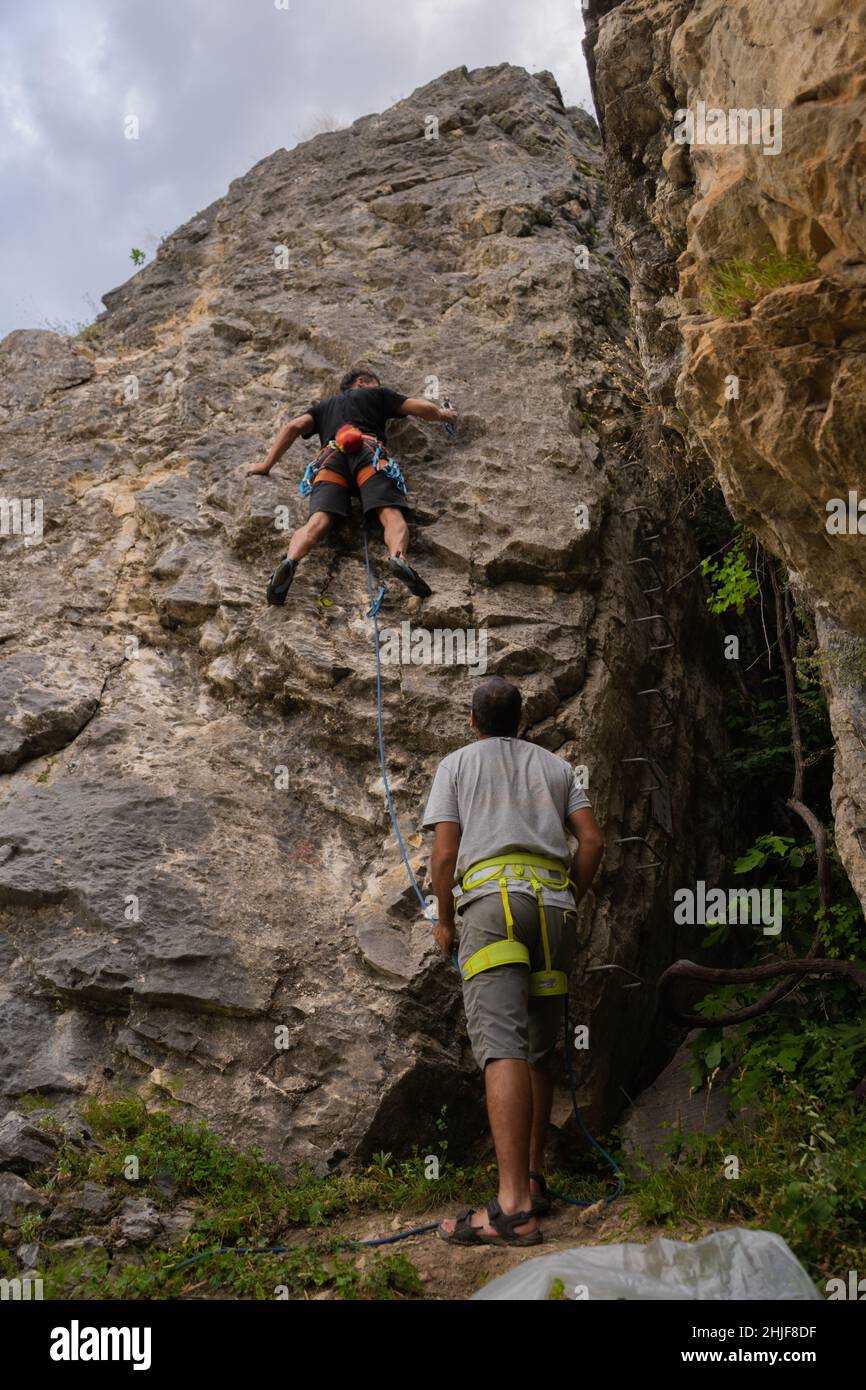 Handsome and fit senior guy is climbing the rocks alone with the rope ...