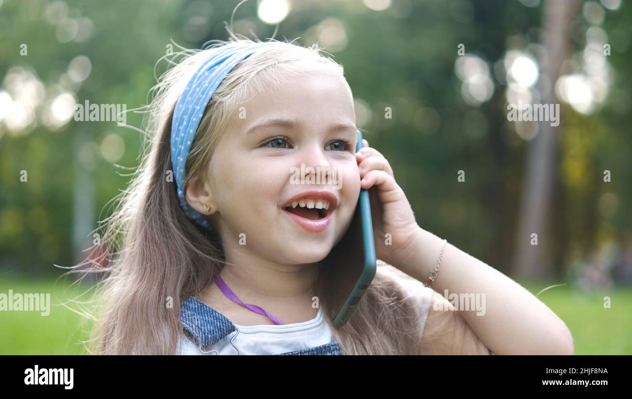 Happy little girl having conversation talking on mobile phone in summer ...