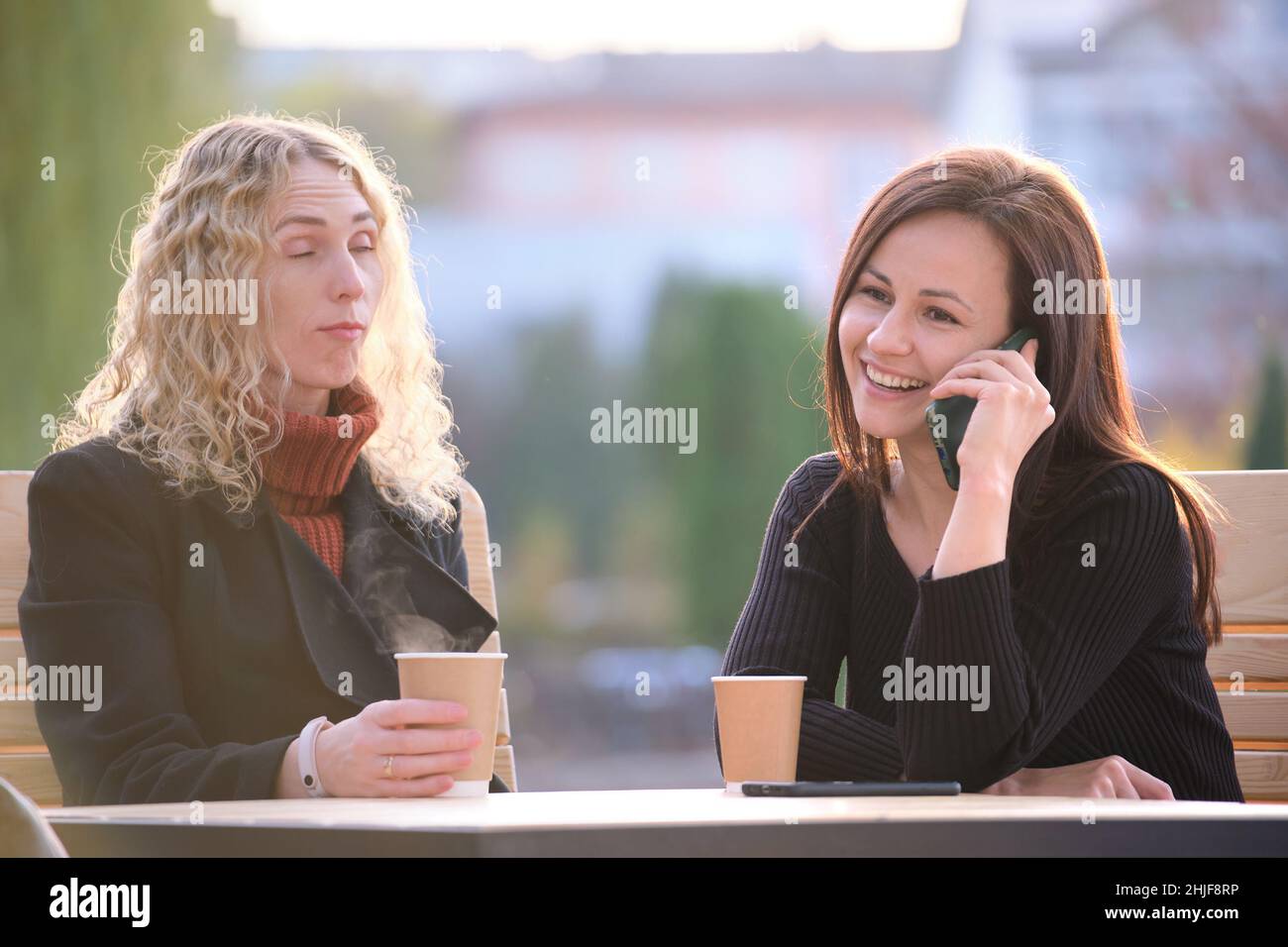 Happy young woman chatting on mobile phone ignoring her bored friend ...