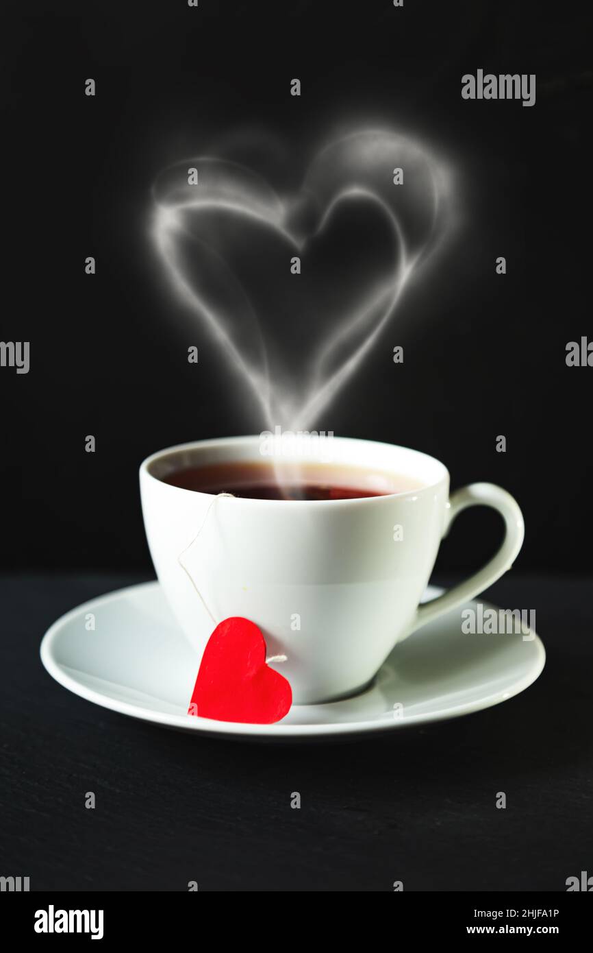 White cup of tea with heart shaped smoke. Black background, selective ...