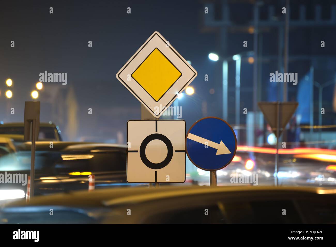 Roundabout road signs with blurred cars on city street traffic at night ...