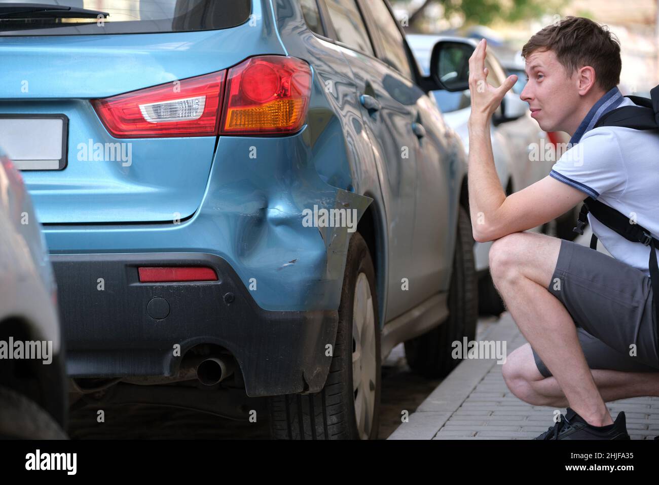Sad male driver sitting on street side shocked looking at his dented ...