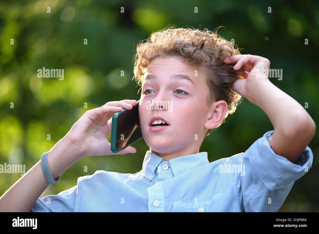 Young puzzled child boy talking on cellphone outdoors in summer park ...