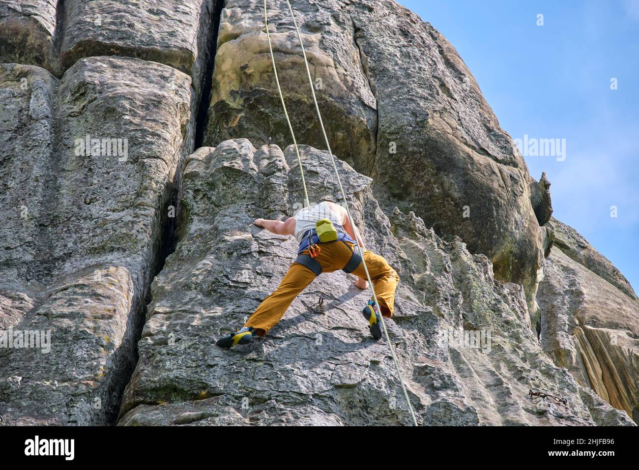 Young man climbing steep wall of rocky mountain. Male climber overcomes ...