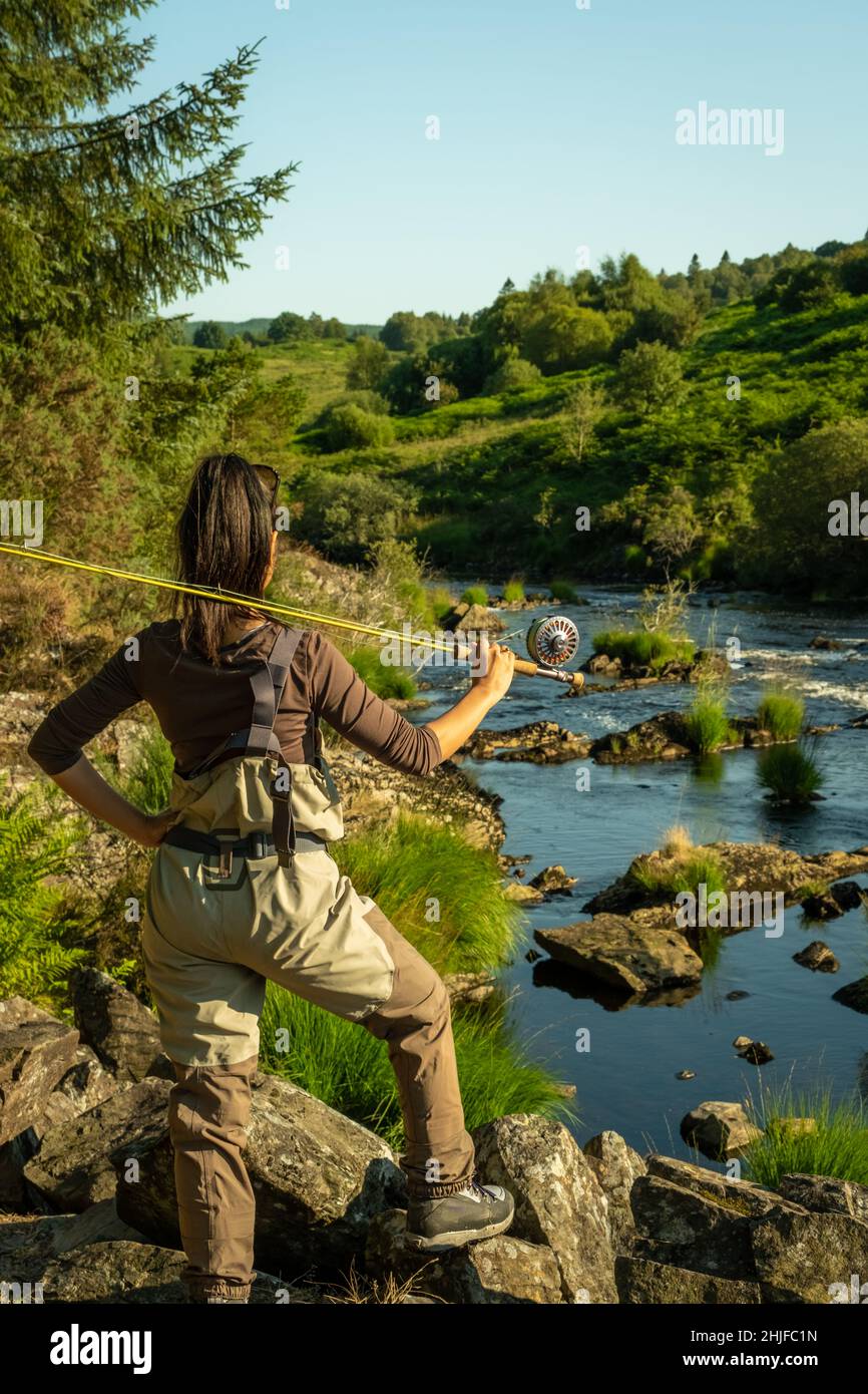 An asian female fly fisher women wearing waders and resting a rod on ...