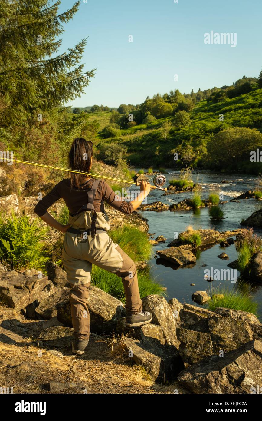An asian female fly fisher women wearing waders and resting a rod on ...