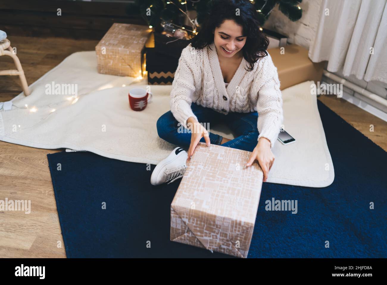 Cheerful woman opening present while sitting on floor Stock Photo - Alamy