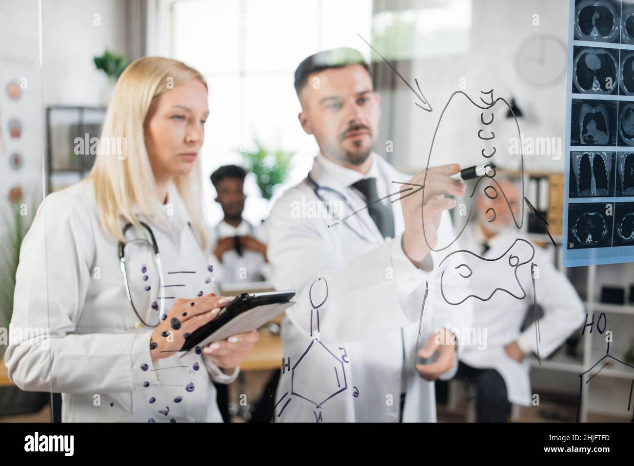Team of qualified medical scientists using tablet and writing on glass ...