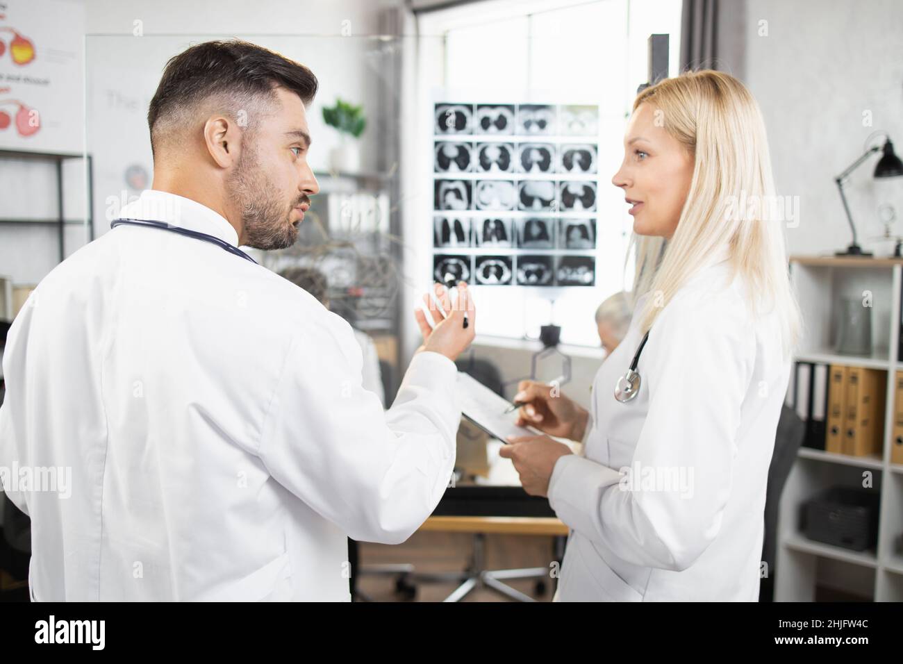 Two qualified doctors in lab coats standing near glass flip chart and ...