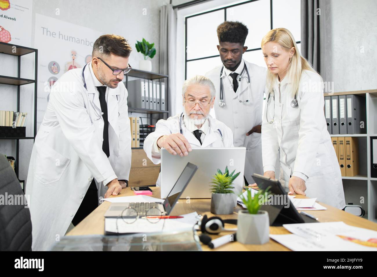Multiracial therapists standing around aged professor that sitting at ...