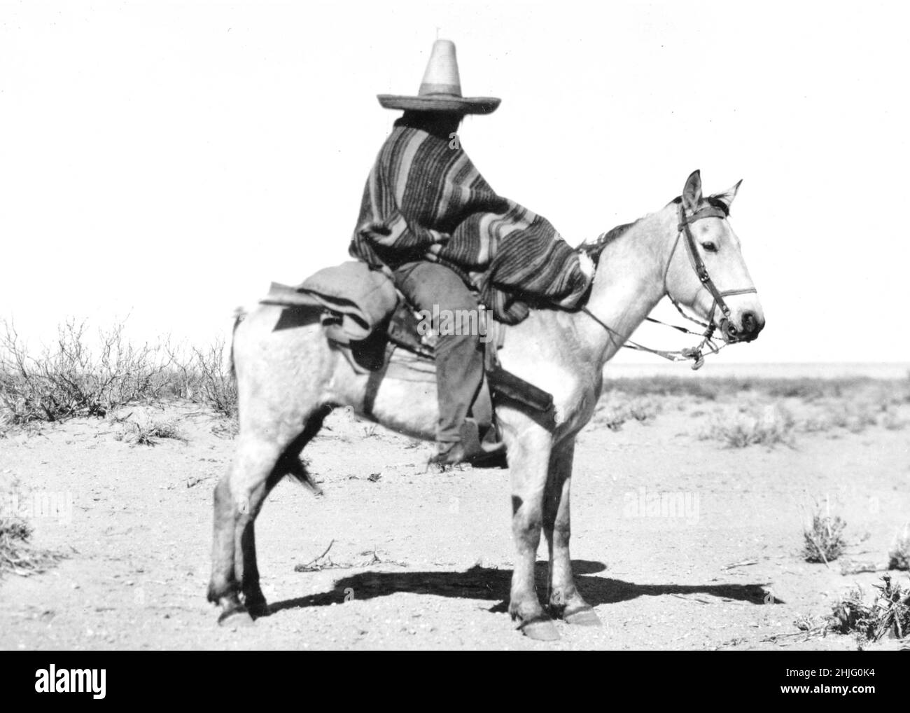 Photograph shows a man on horseback in desert terrain, wearing a serape ...