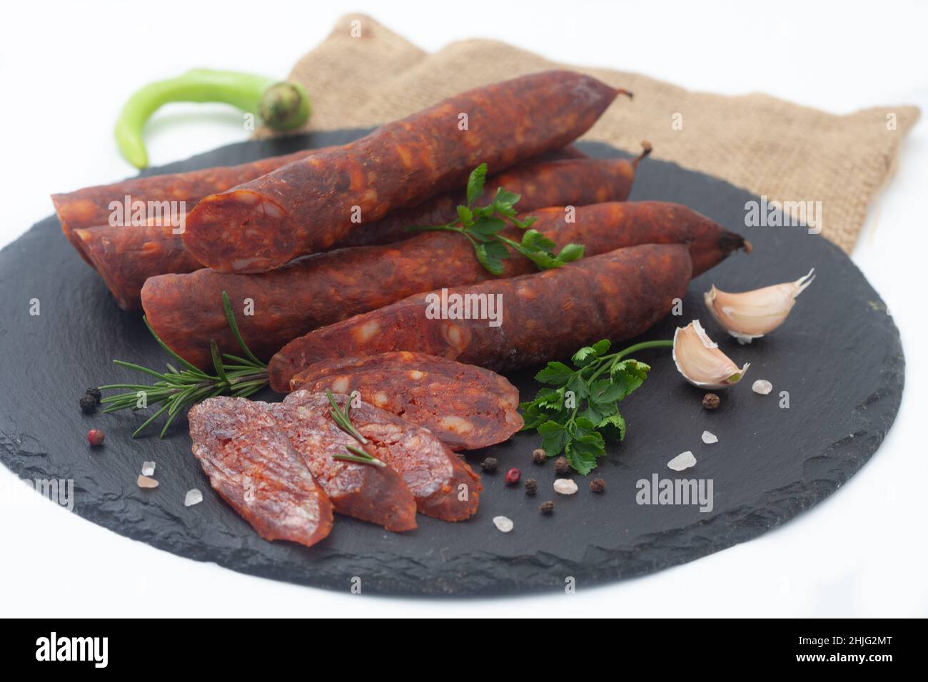 Dry sausages made of pork meat on a black board with fresh herbs and ...