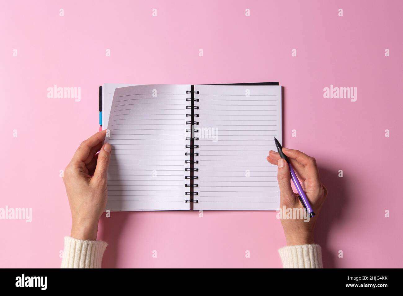 Female hand writing in blank open spiral notebook with pen on pastel ...