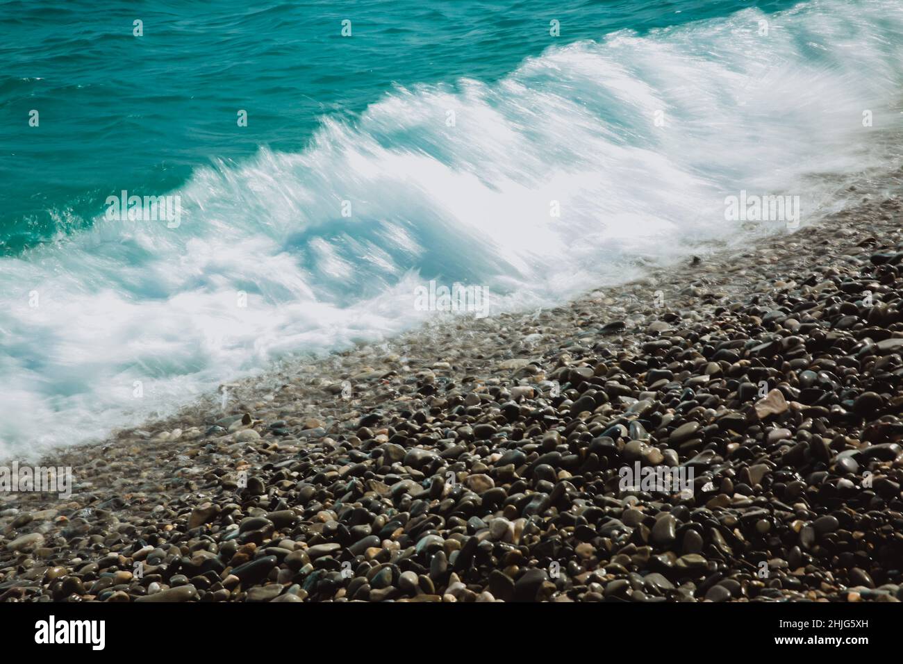 Wet black pebble beach covering with frothy water of waves. Background ...