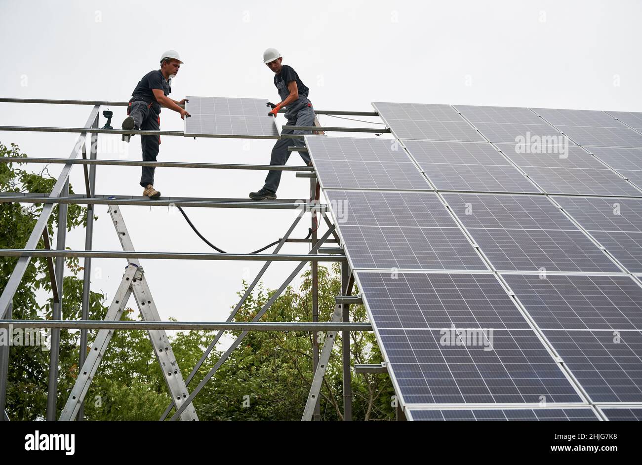 Workers installing solar panels on metal beams. Men wear helmets and ...