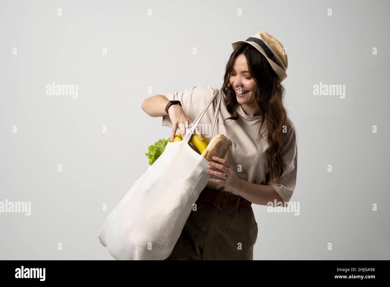 Smiling young woman in beige t-shirt and a hst with a mesh eco bag full ...