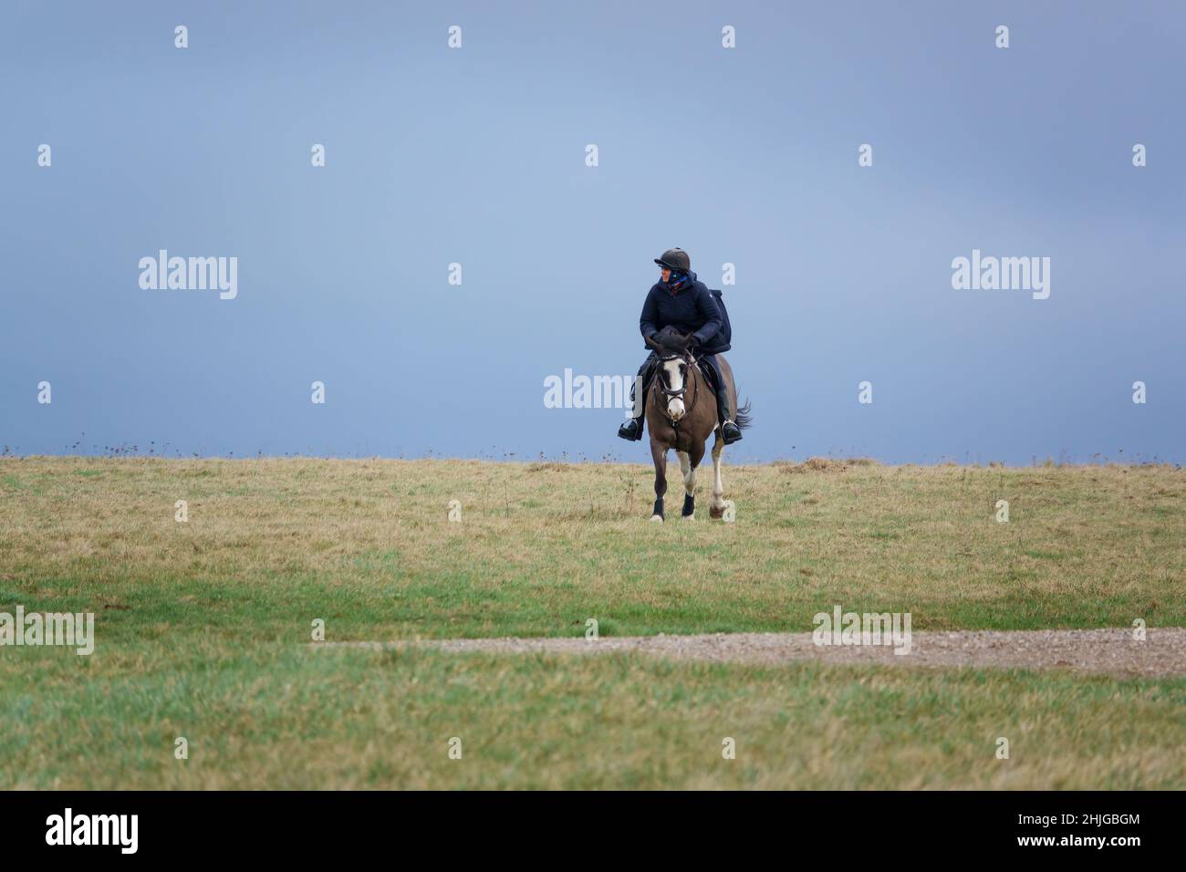 lady horse riding in open countryside under a blue grey cloud winter ...